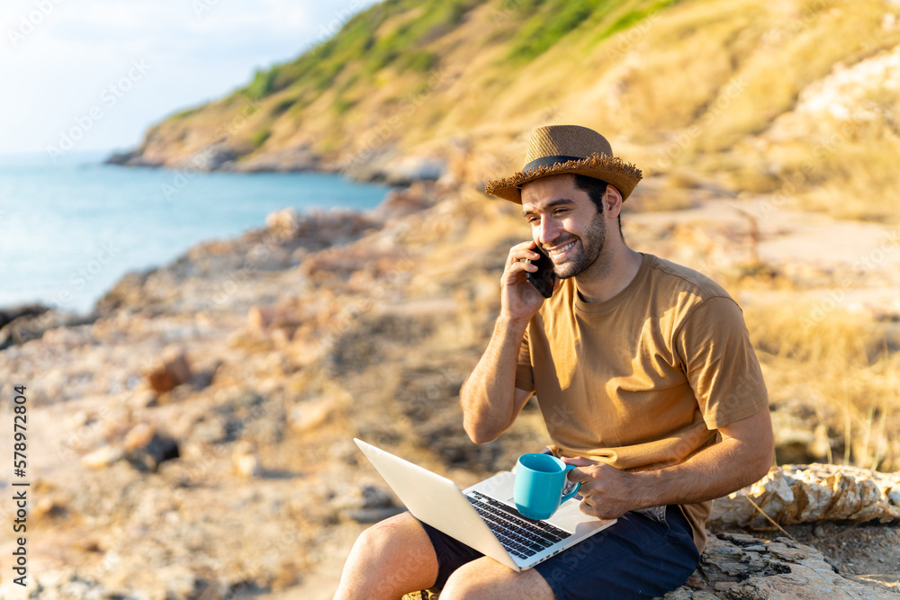 Caucasian man freelancer sitting on coastline hill working on laptop ...