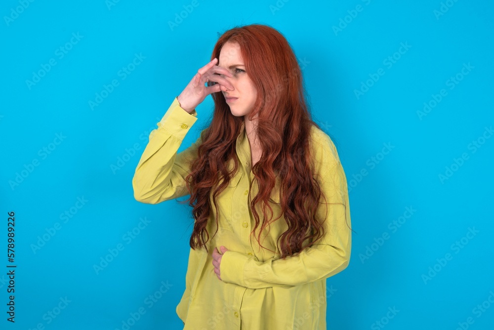 young woman wearing green sweater over blue background smelling ...