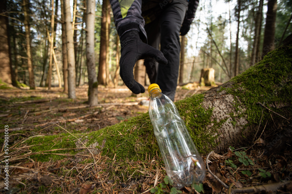 Unrecognizable man crouching down to pick up a discarded empty plastic ...