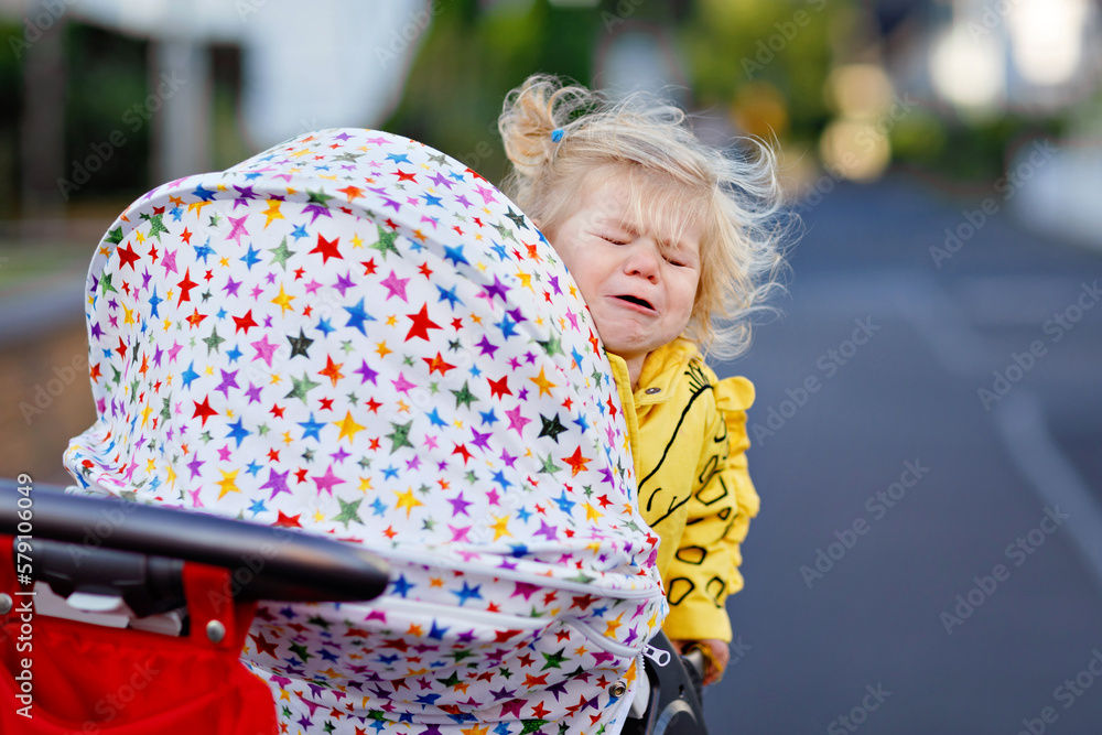 Portrait of little sad toddler girl sitting in stroller and going for a ...