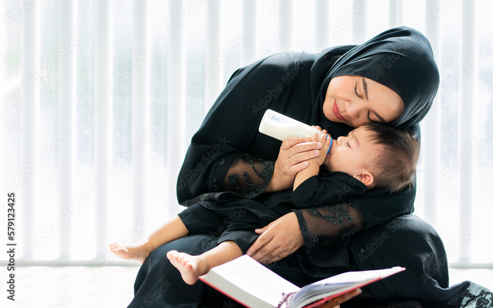 Muslim mother wearing traditional black dress and headscarf, carrying ...