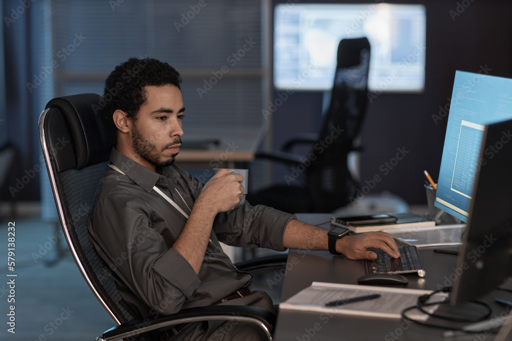 Side view portrait of man using computer and drinking coffee while ...