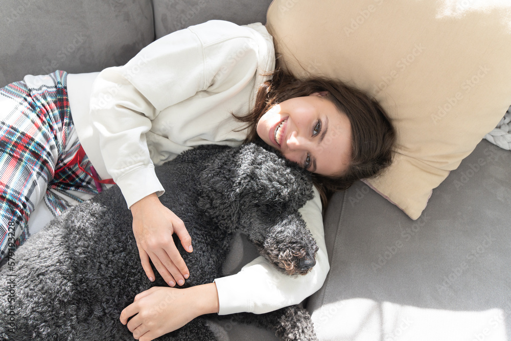 Happy teenage girl and her dog cuddling together on living room sofa ...