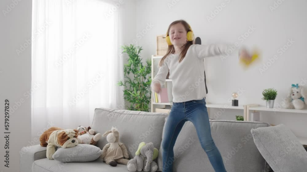 Hyperactive little girl jumping and dancing on sofa. Kid listening to ...