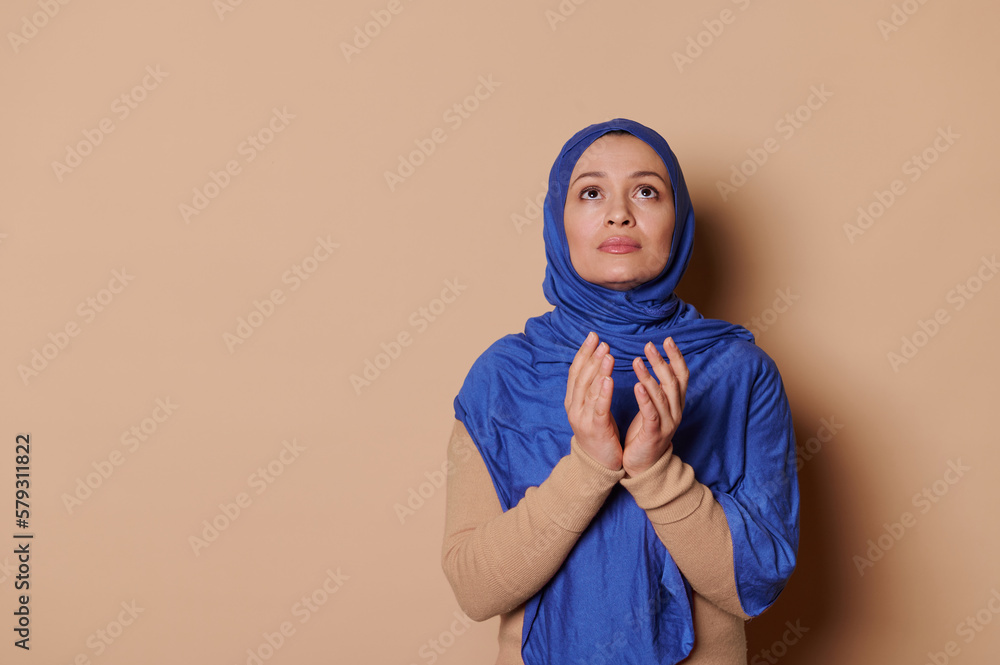Peaceful Arab Muslim woman in blue hijab, looking up with gratitude ...