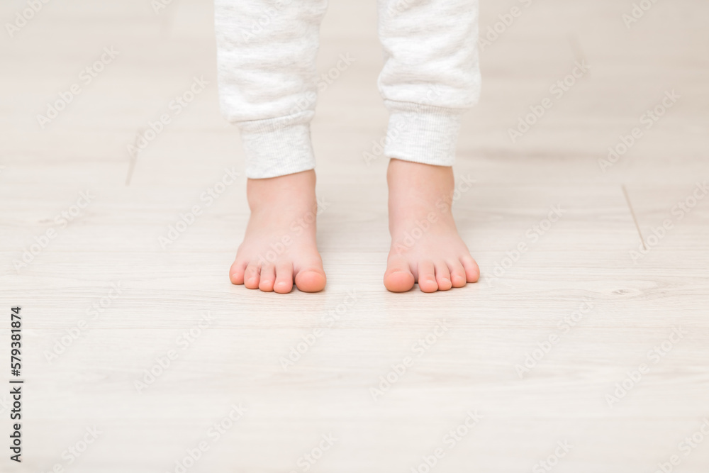 Little child legs in white warm trousers standing on light beige wooden ...
