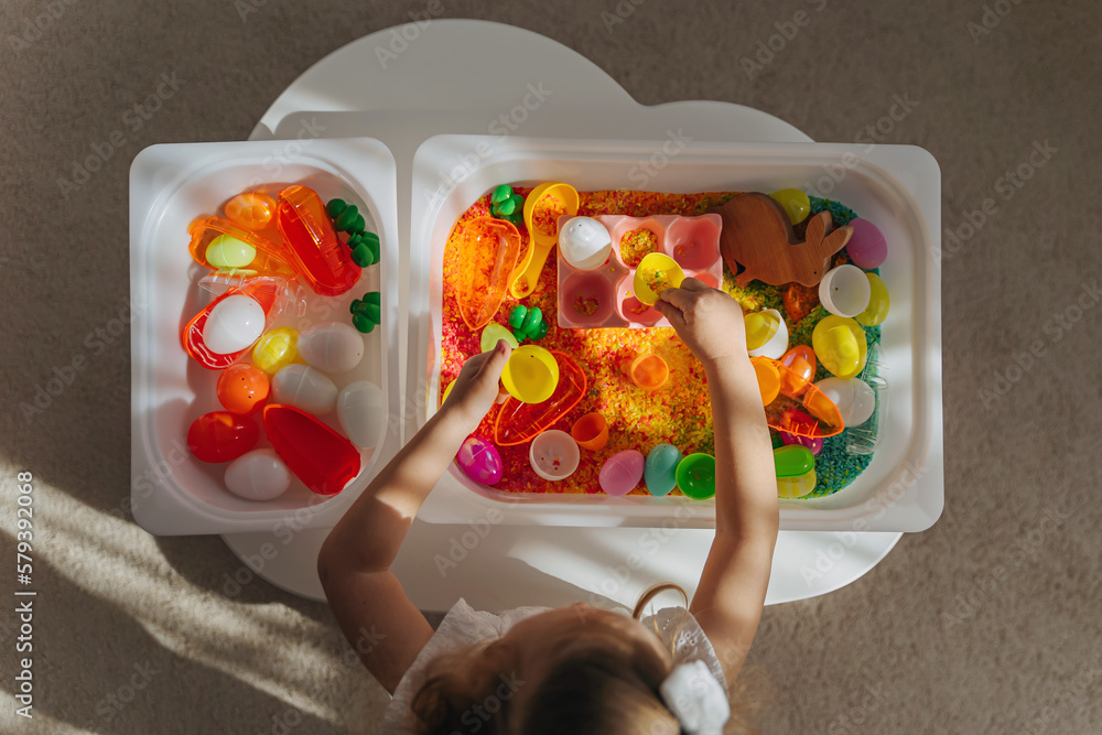 Child playing with colored rice and Easter eggs in sensory bin. Easter ...