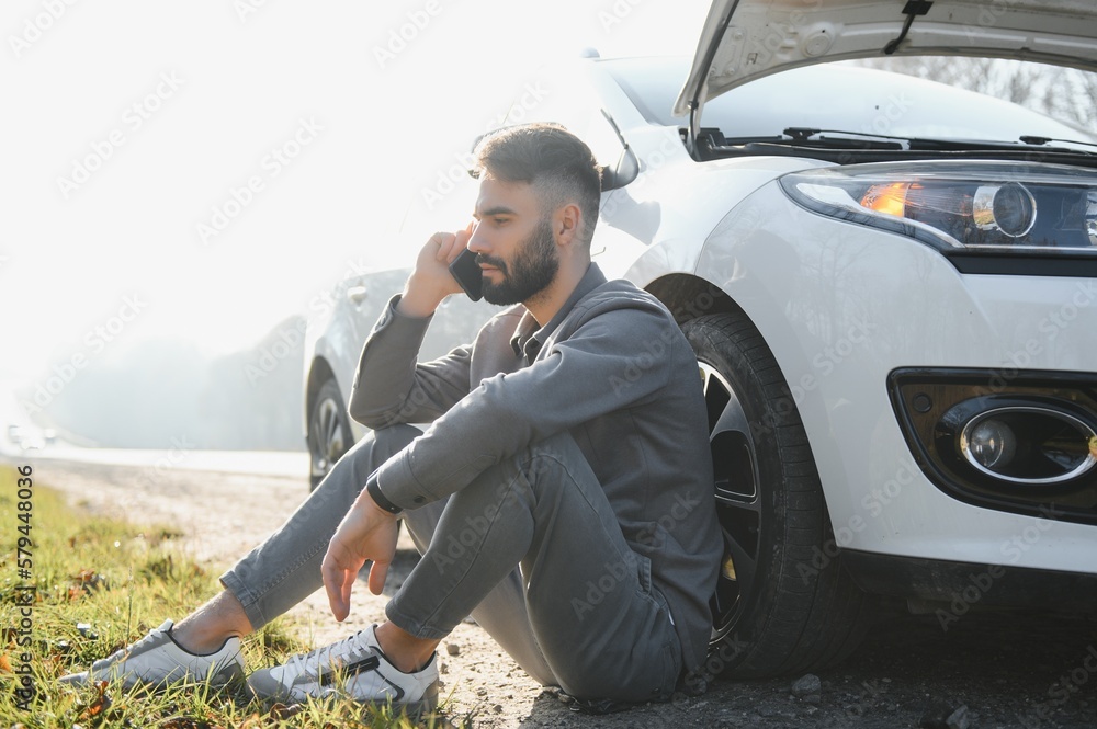 Foto de Frustrated sad upset guy driver is sitting near a broken car ...