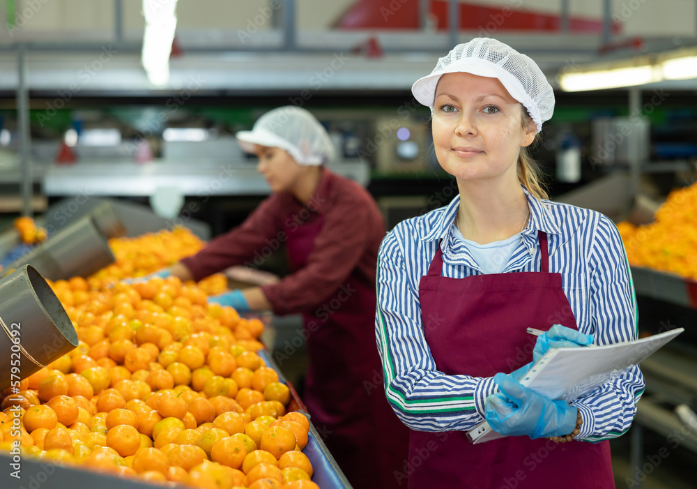 Smiling female shift supervisor standing with papers in hands near ...