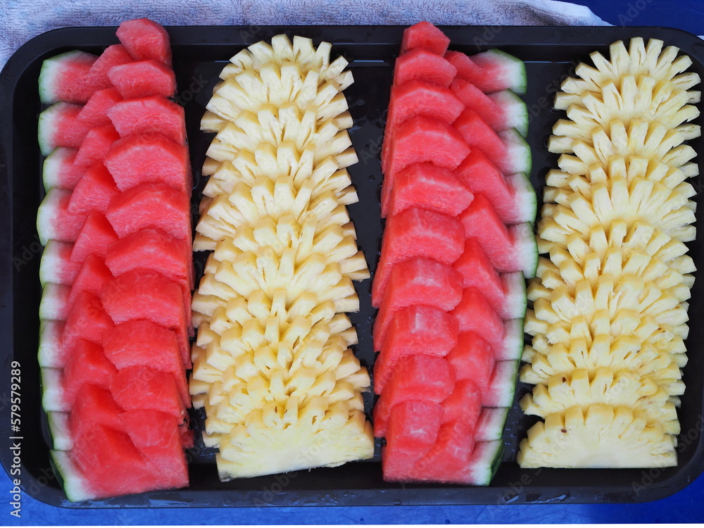 Watermelon and pineapple slices beautifully arranged in a black plastic tray served as fruit ...