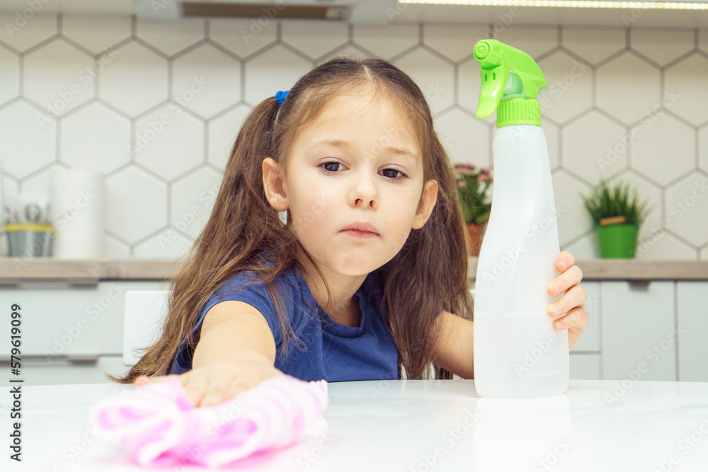 Pretty little girl with detergent sprayer and household rag wipe table ...