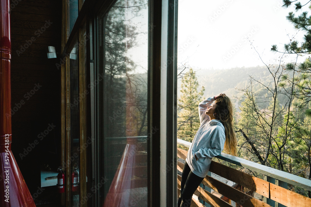 Side view of young woman with hand in hair standing on balcony in log ...