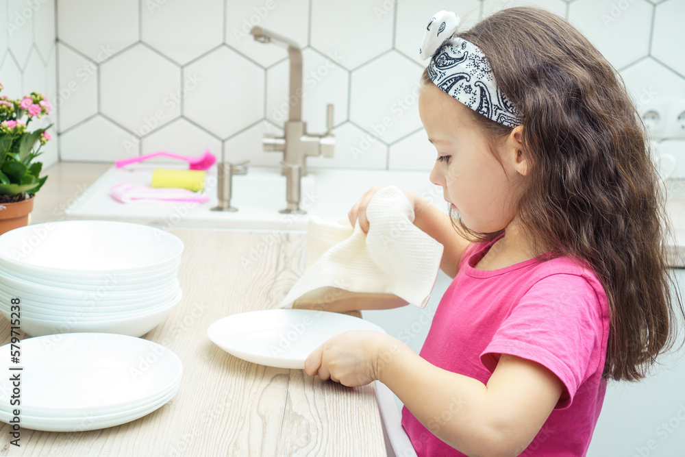 Pretty little girl wiping clear white plates with dry towel on kitchen ...