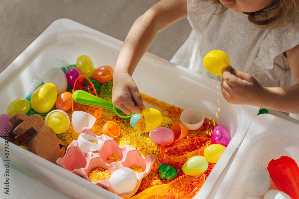 Child playing with colored rice and Easter eggs in sensory bin. Easter ...