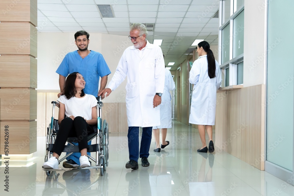 Doctor and male nurse transport a female patient in a wheelchair along ...