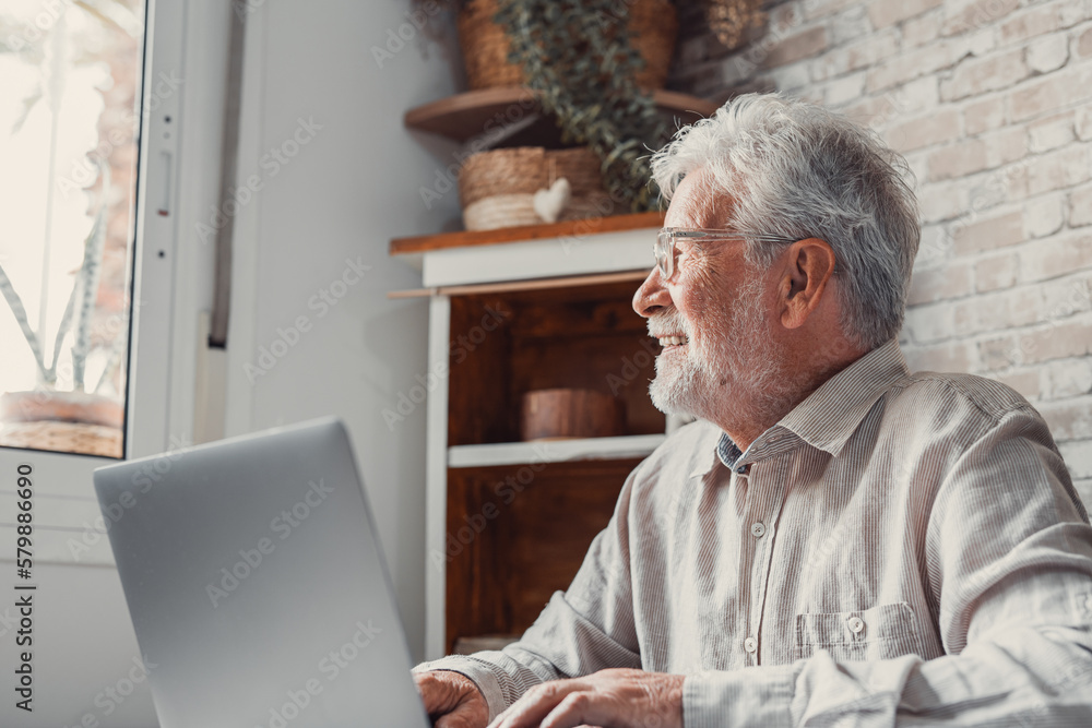 Smiling mature 70s man in glasses sit at table working on laptop look ...