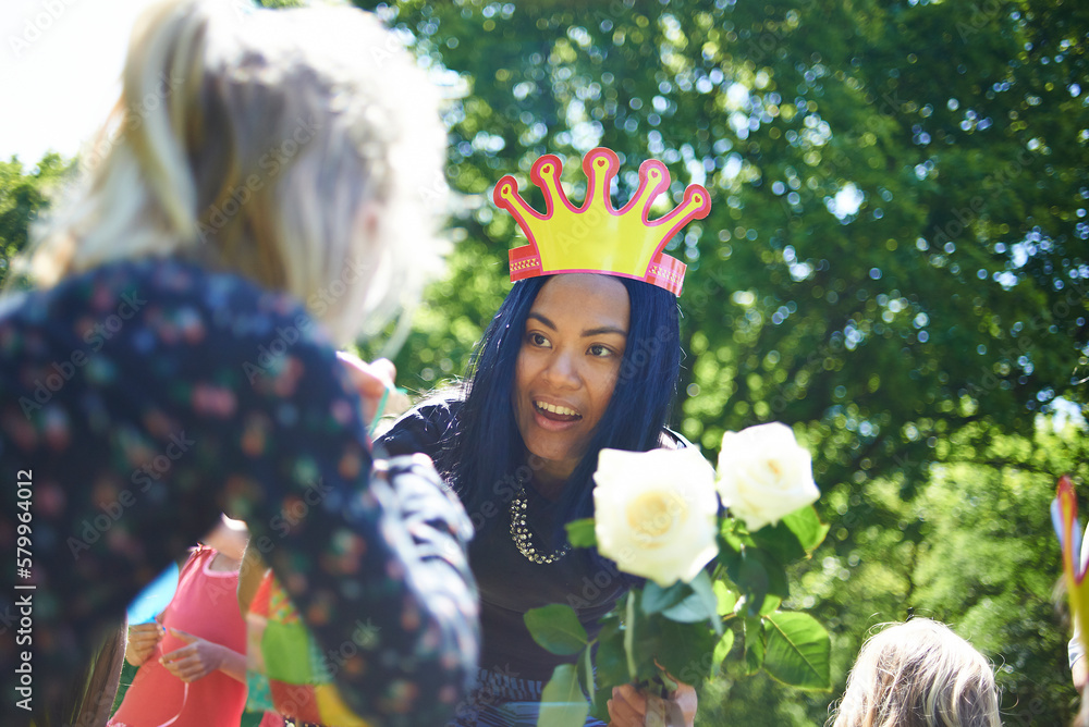 Happy woman wearing paper crown while giving white roses to teenage ...