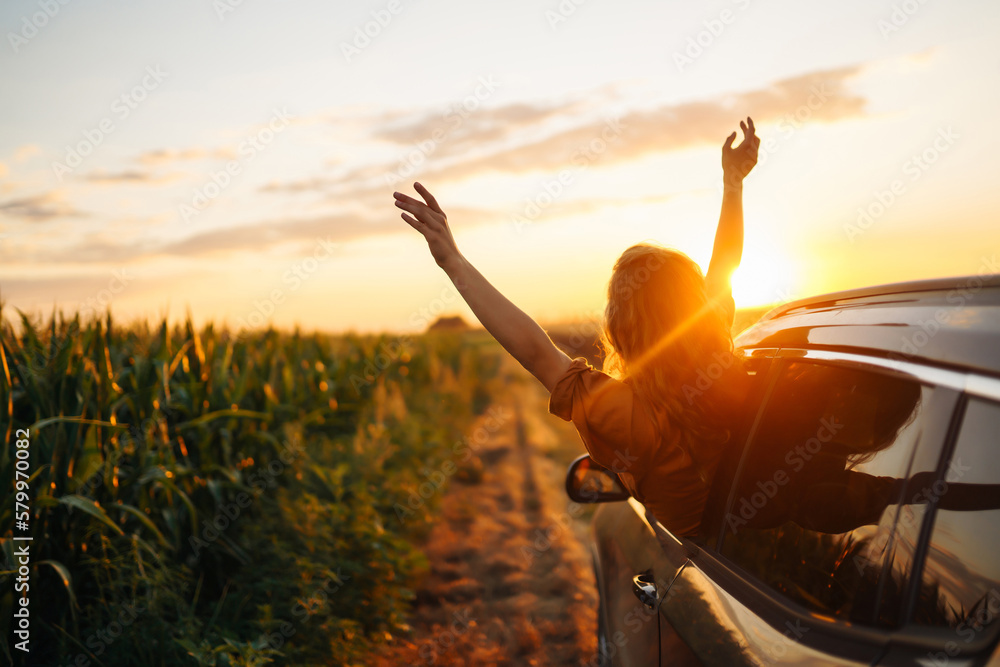Happy woman outstretches her arms while sticking out the car window ...