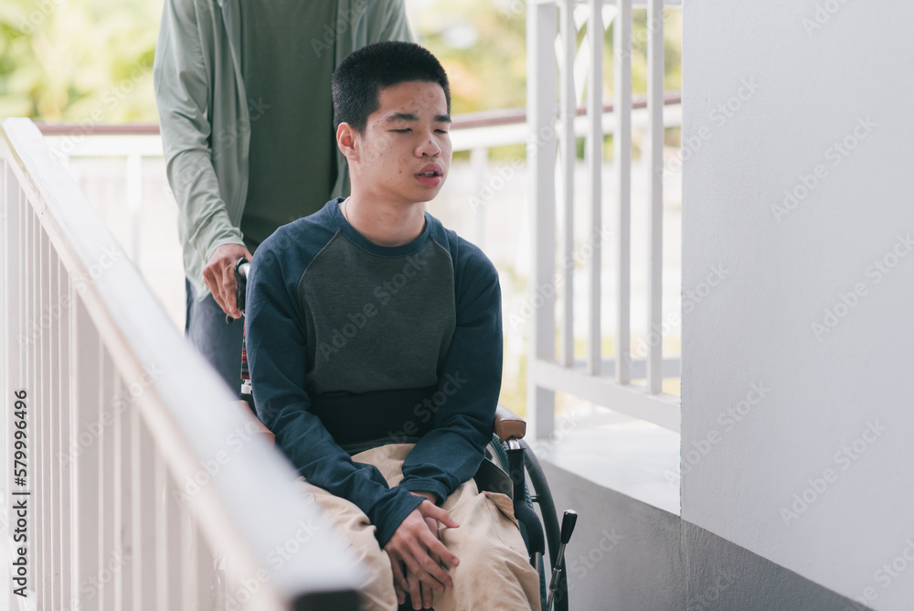 Teenage boy sit in a wheelchair that is pushed by a caregiver or ...
