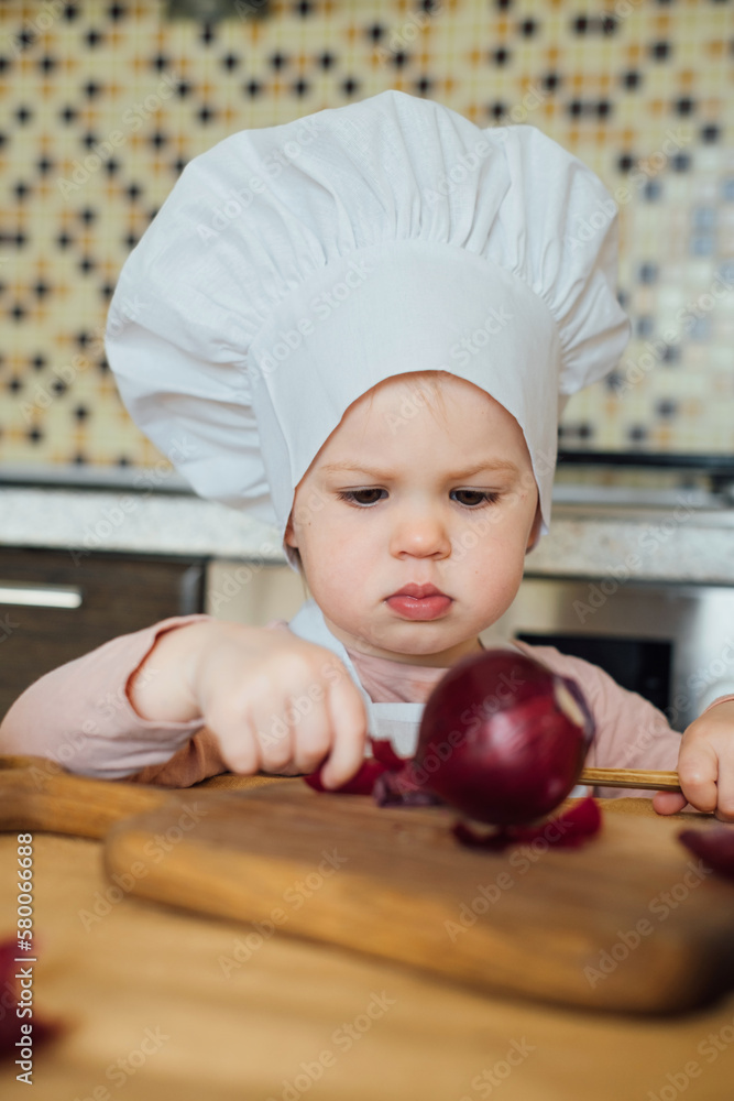 Little girl cooking in the kitchen wearing an apron and a Chef's hat ...