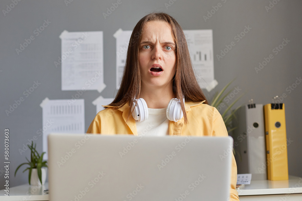 Image of surprised shocked scared woman wearing yellow shirt sitting in ...
