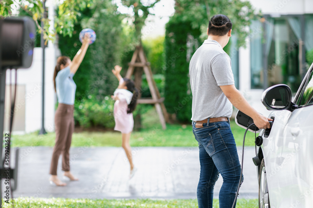 Focus image of progressive man charging electric car from home charging ...