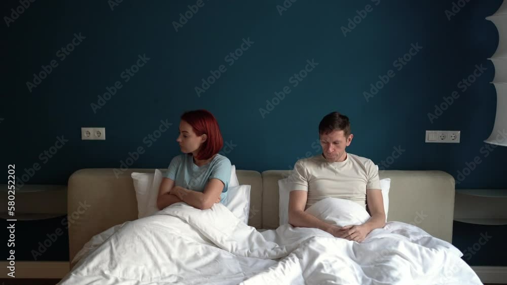 Unhappy millennial family couple sitting in bed not talking, ignoring ...