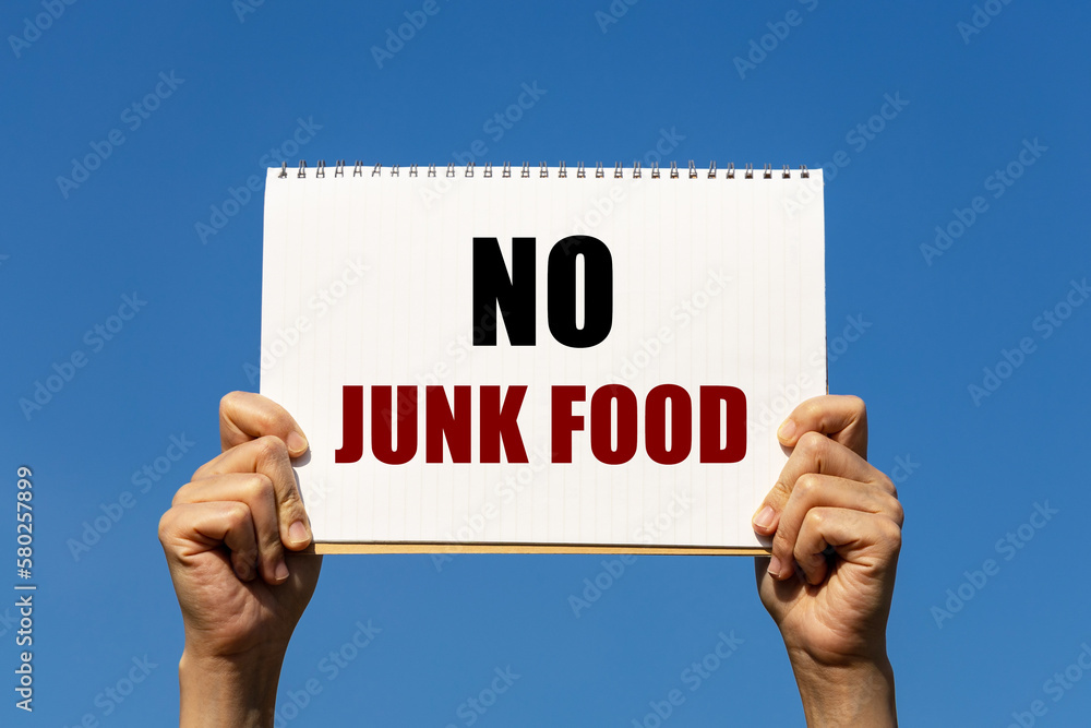 No junk food text on notebook paper held by 2 hands with isolated blue ...