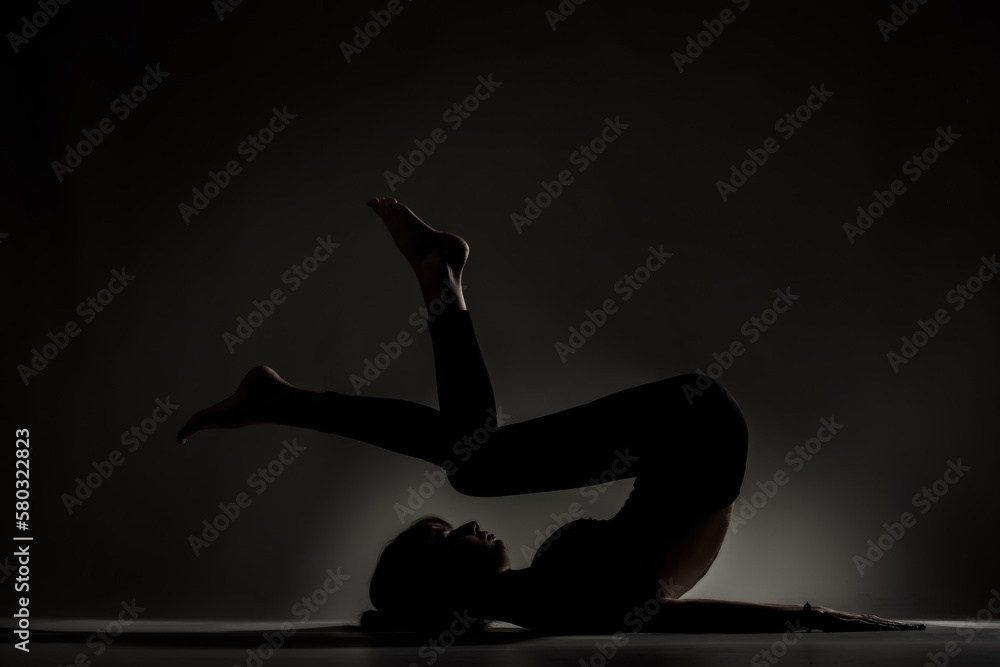 Fit ballerina girl lying and stretching practicing yoga poses. Side lit ...