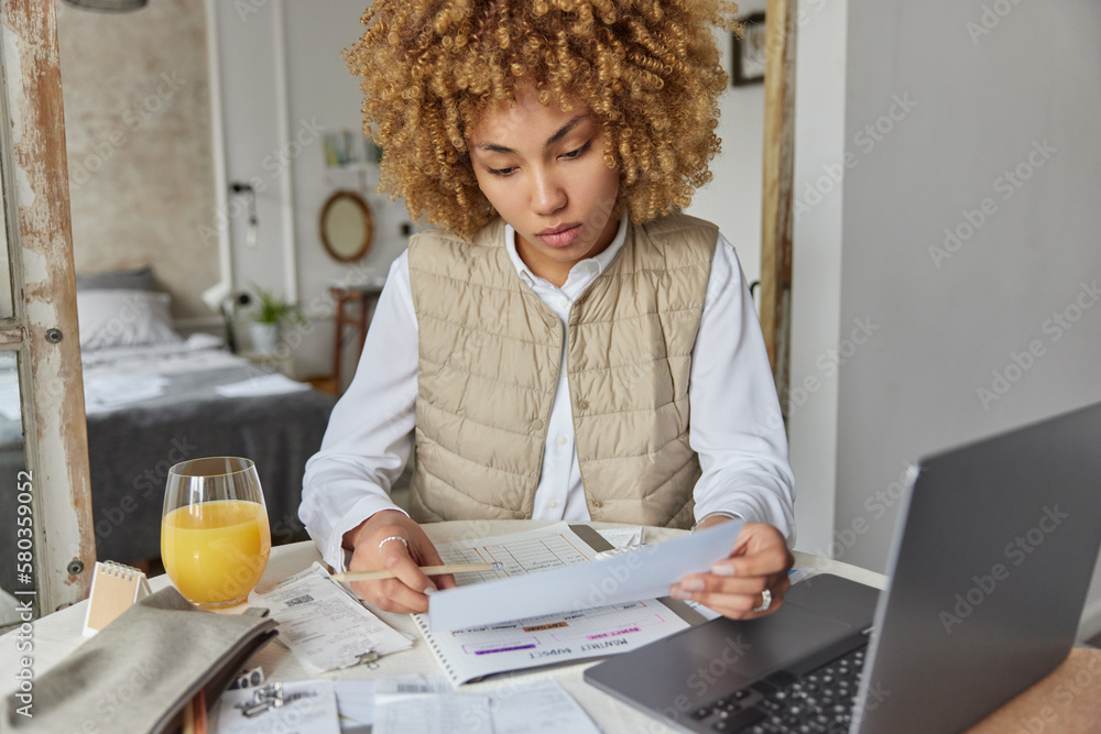 Female model sits at desktop plans budget holds paper studies receipts ...