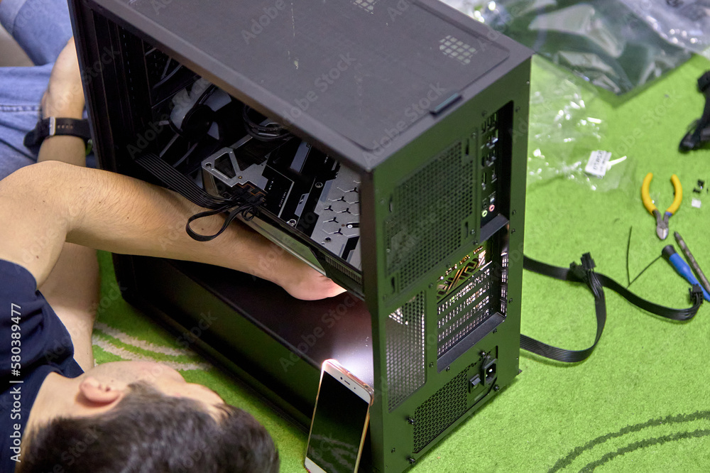 young guy, shines a flashlight on his phone, assembles a new computer ...