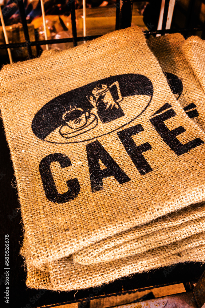A stack of empty tan jute coffee sacks with ' Cafe ' printed in black ...