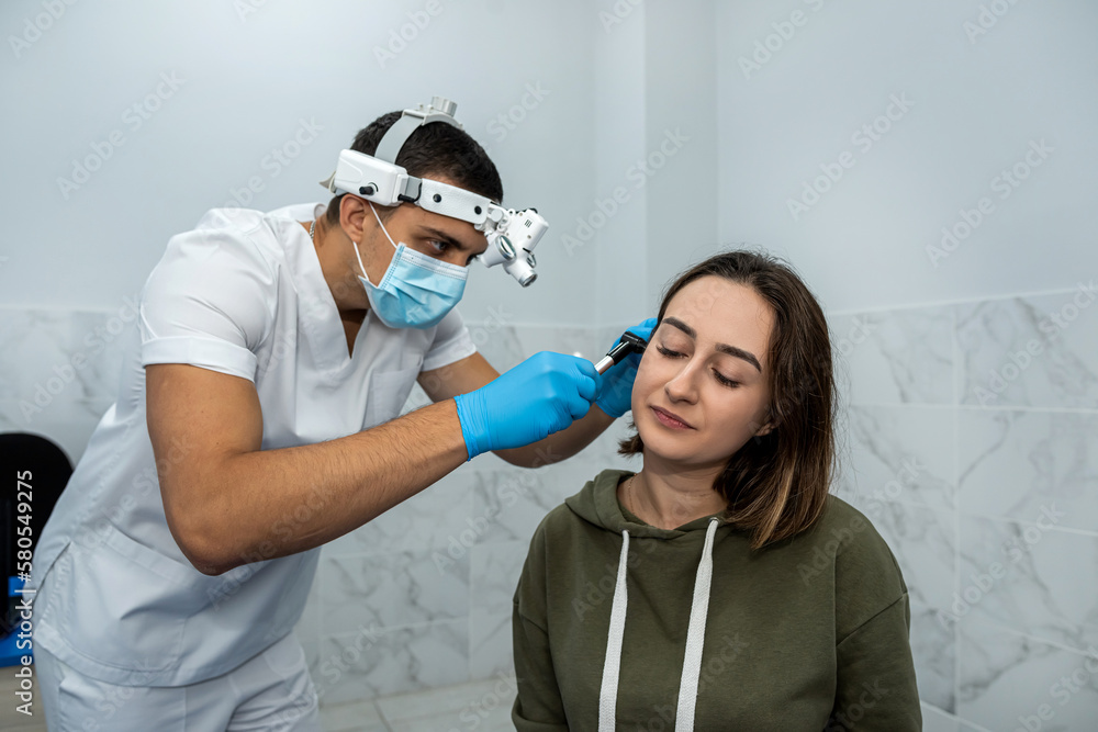 ENT doctor examines the ear with an otoscope of a female patient in the ...