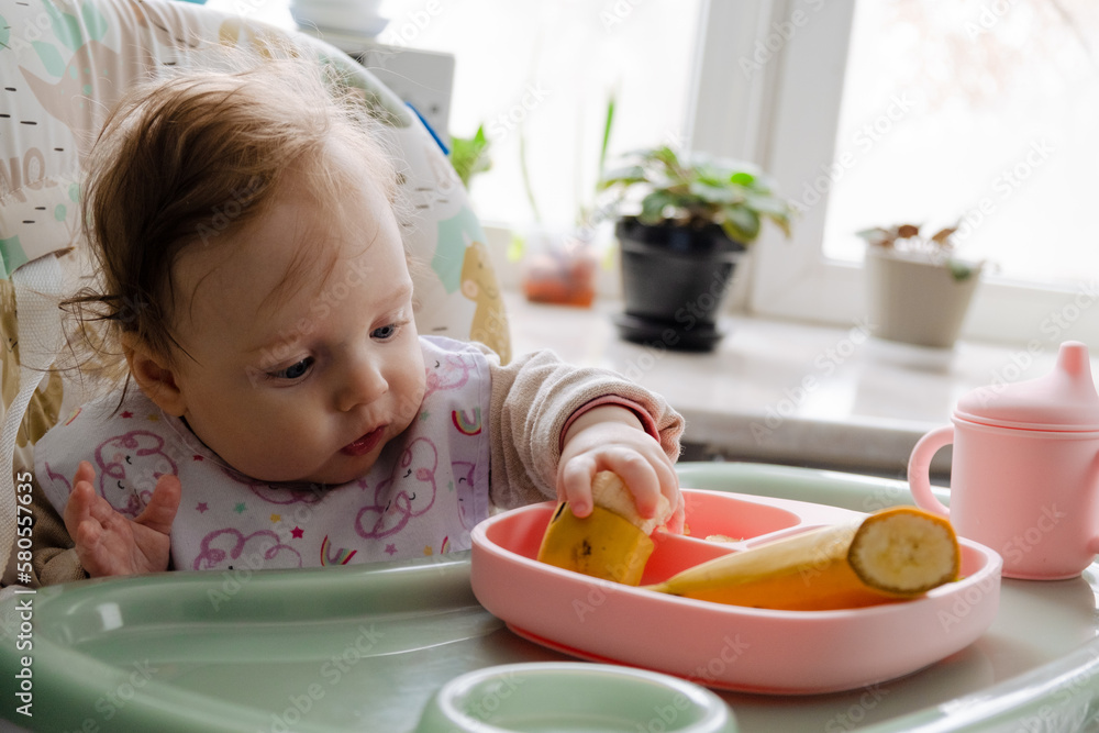 Cute baby girl tries to eat her first meal. Baby-Led Weaning (BLW ...