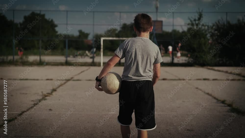 Kid on a ghetto soccer field court playing football and kicking ball ...