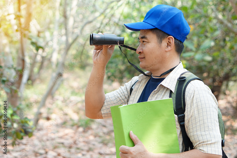 Foto de Asian man explorer wears blue cap, holds binocular in forest to ...