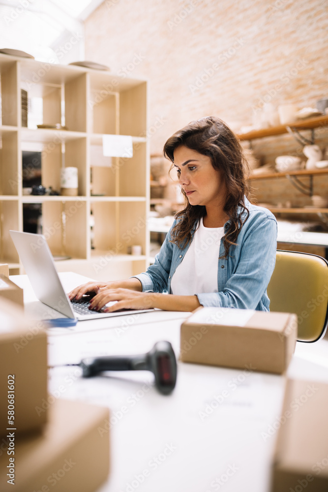 Online store owner using a laptop in a warehouse Stock Photo | Adobe Stock