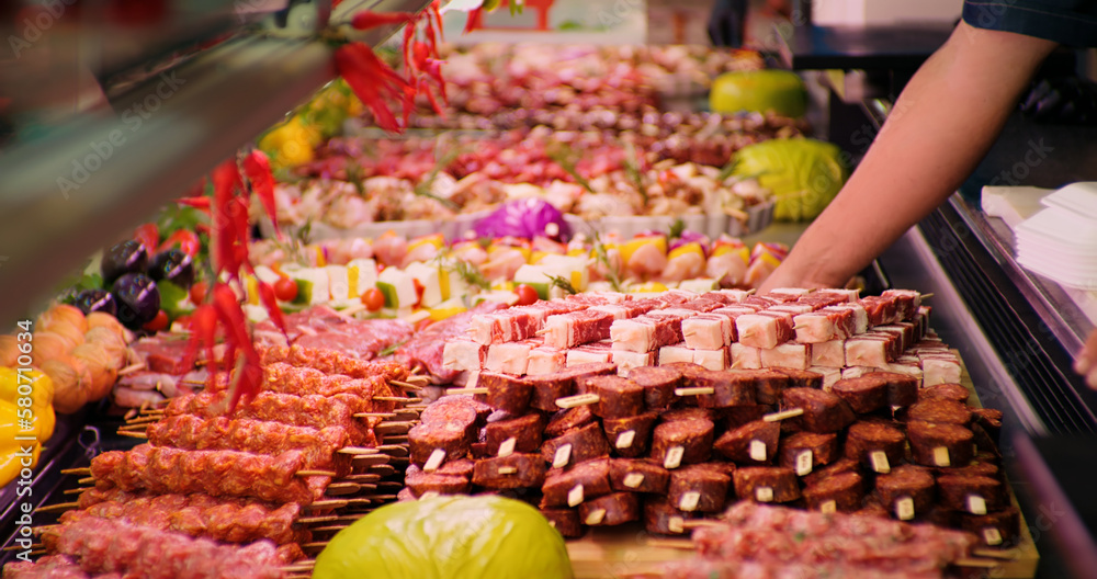 Man hands in gloves placing a tray full of pieces of meat on skewers ...