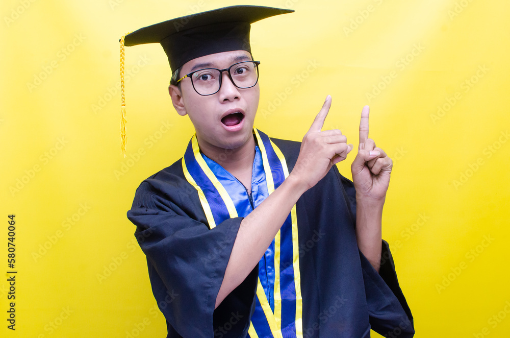 A young Asian man celebrates his graduation by clenching his fist and ...