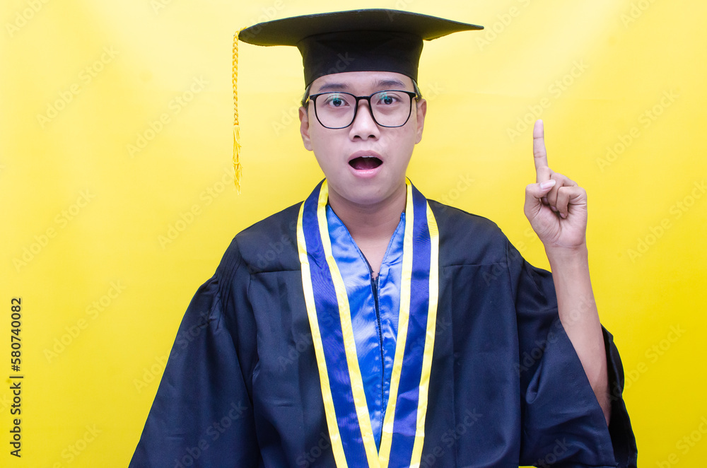 A young Asian man celebrates his graduation by clenching his fist and ...