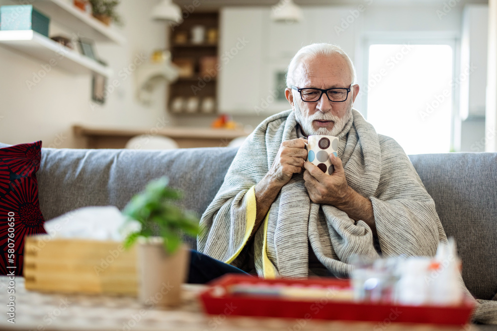 Sick older man with headache sitting under the blanket in the living ...