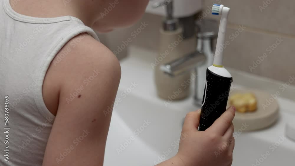 kid boy washing teeth with electric in bathroom looking in mirror and ...