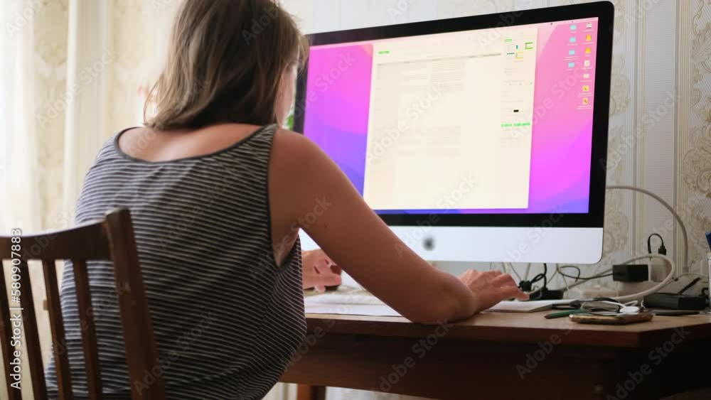 Rear view of a desktop and a woman sitting behind it working at a ...