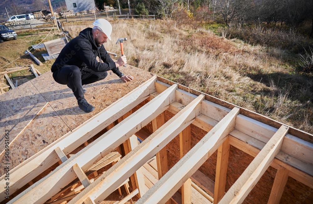 Carpenter hammering nail into OSB panel on the roof top of future ...