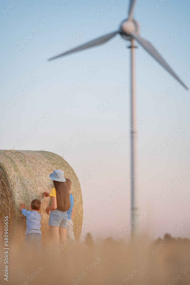 Children with a coil of hay on the background of a wind turbine. Little ...