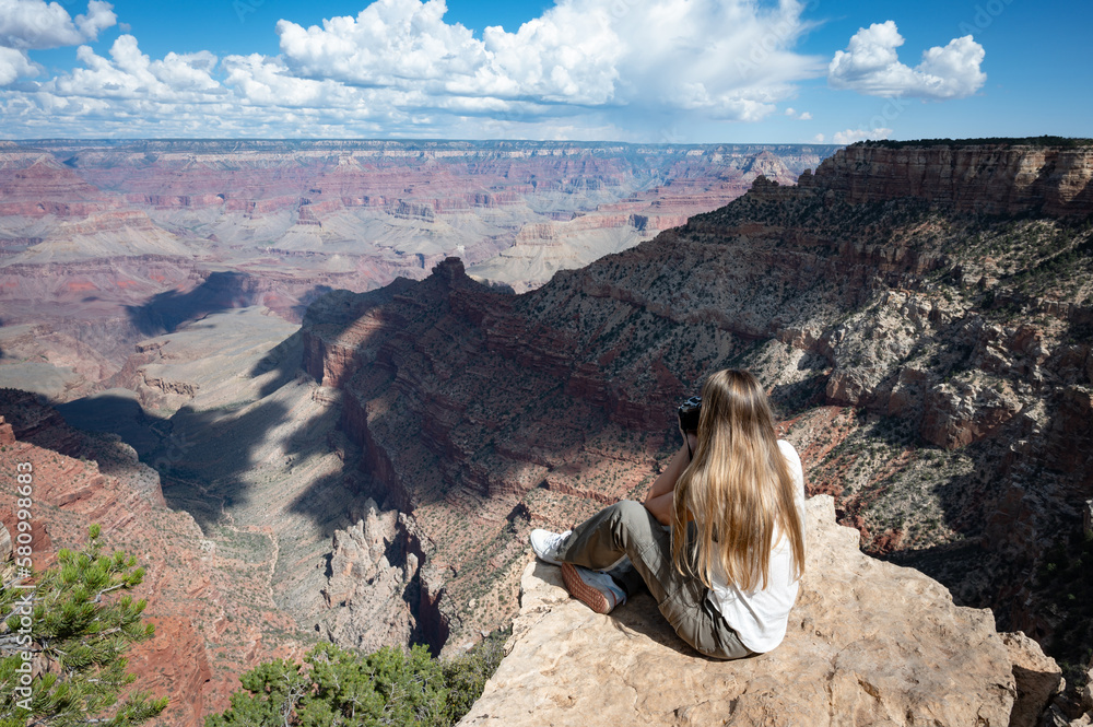 Long-haired blonde young girl sitting on the edge of the cliff of the ...