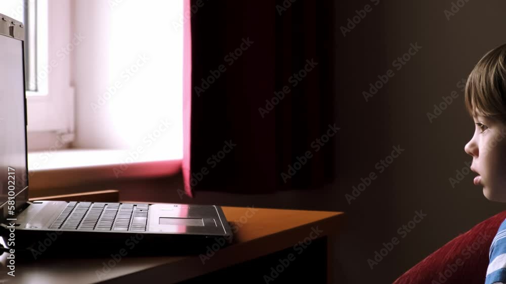 The boy looks into laptop. Child watching cartoons. Closeup face ...
