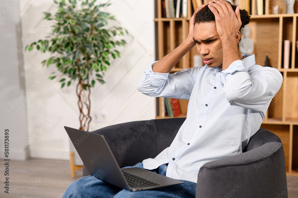 Confused multiracial man in smart casual shirt looking at the laptop ...