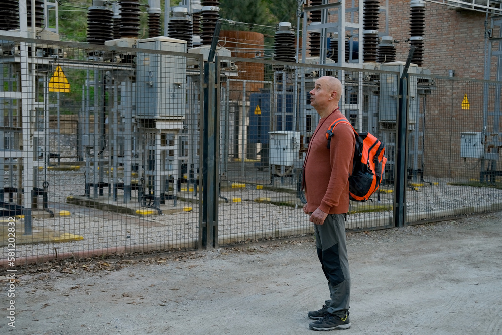 mature man, backpacker looks at power plant, station, substation ...