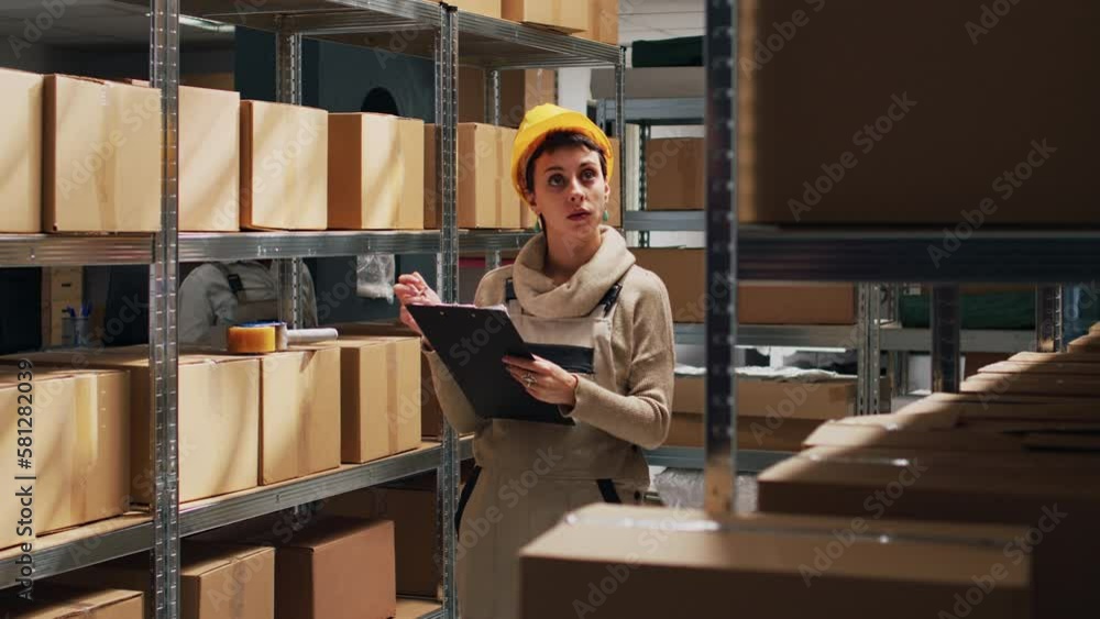 Young woman writing stock logistics in warehouse, looking at cardboard ...